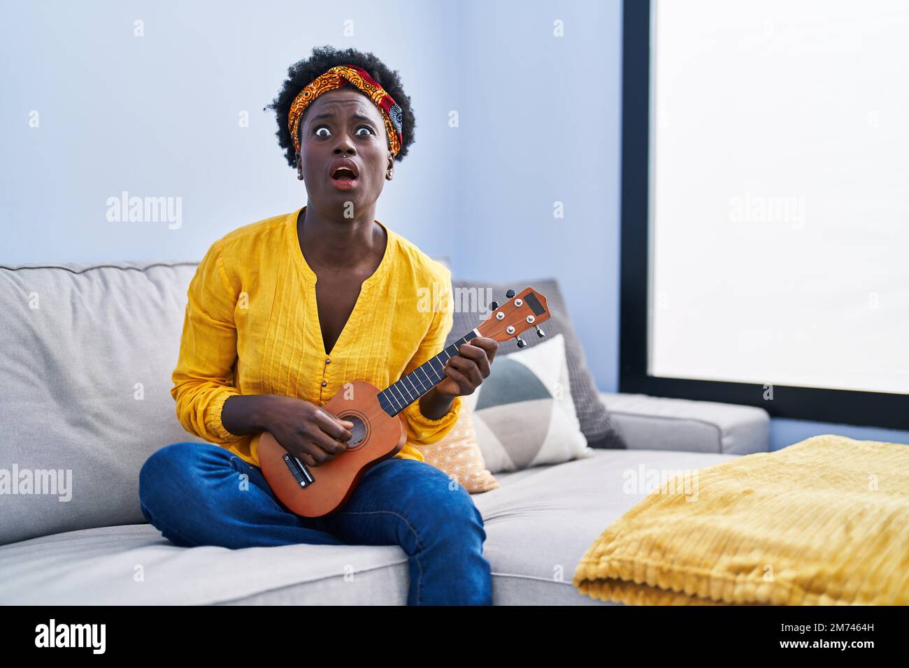 African young woman playing ukulele at home angry and mad screaming ...