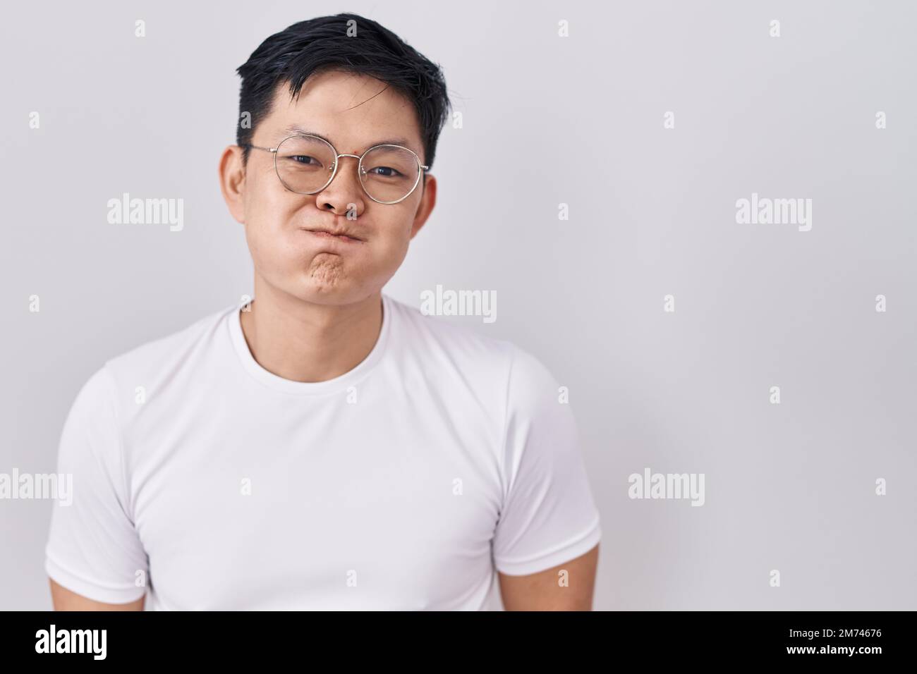 Young asian man standing over white background puffing cheeks with ...