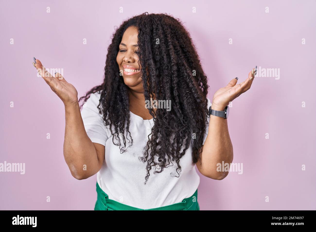 Plus size hispanic woman standing over pink background smiling showing ...
