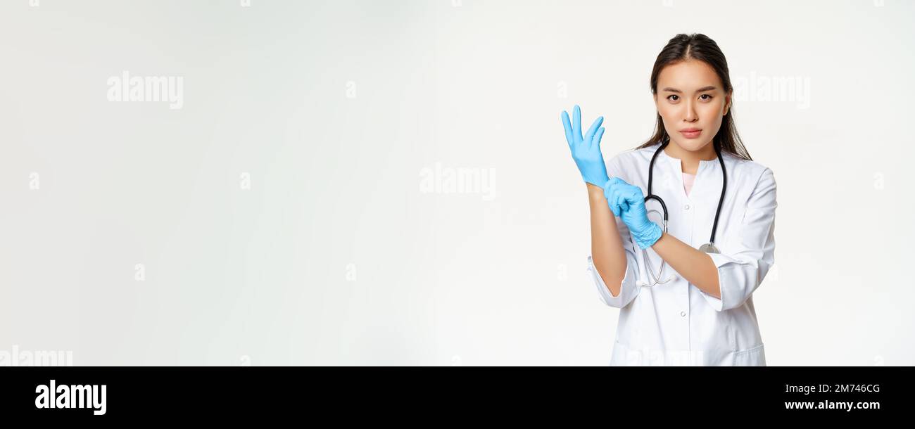 Confident female nurse, physician put on rubber medical gloves for ...