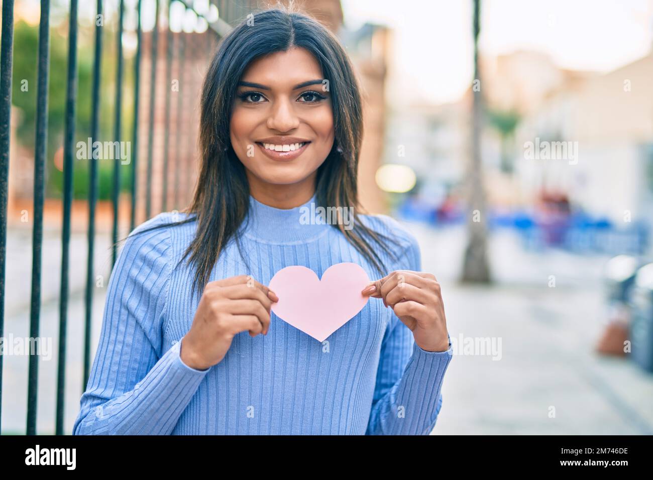 Beautiful hispanic woman smiling holding pink heart at the city Stock ...