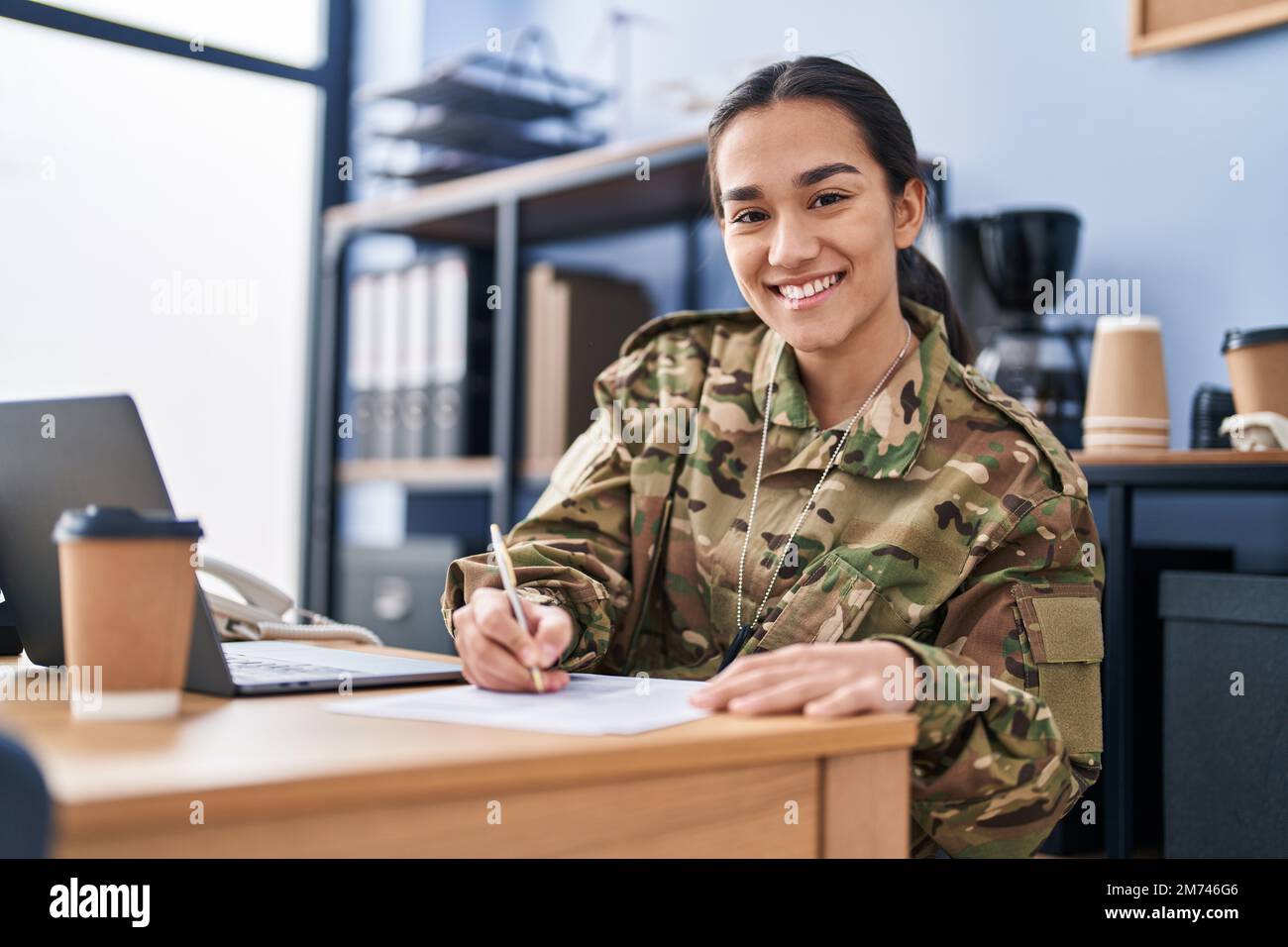 Young hispanic woman army soldier using laptop writing on document at ...