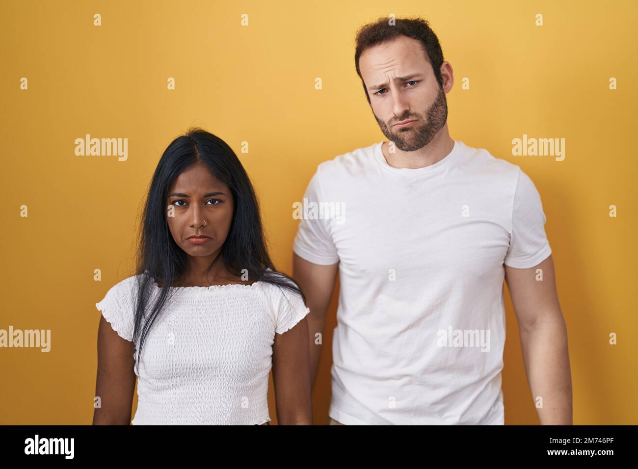 Interracial couple standing over yellow background depressed and worry ...