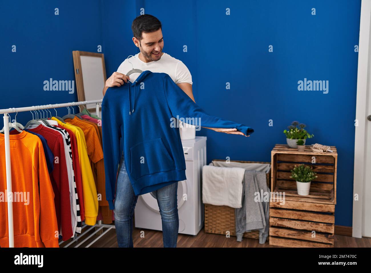 Young hispanic man putting clothes on clothes rack at laundry room ...