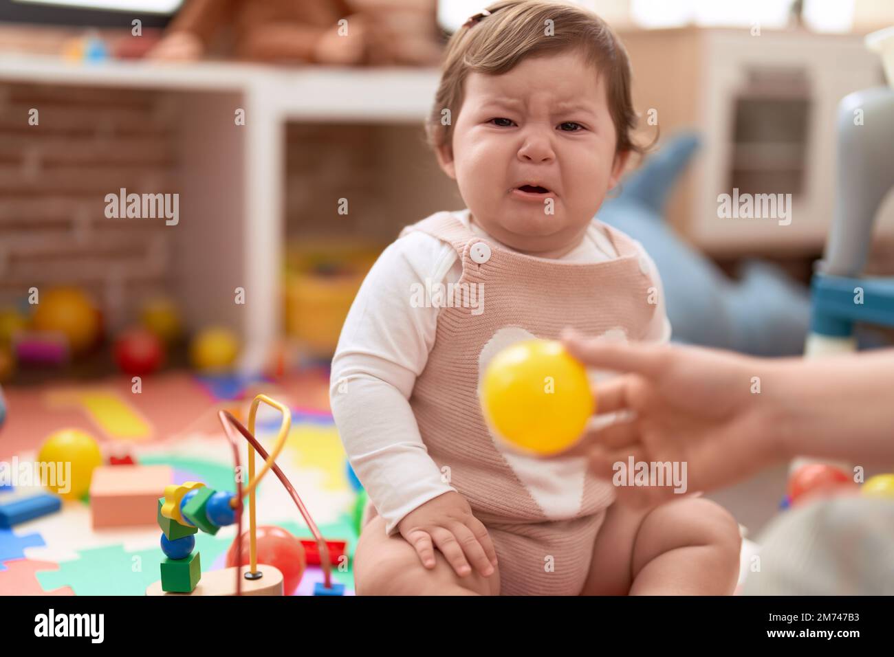 Adorable toddler sitting on floor looking ball crying at kindergarten ...