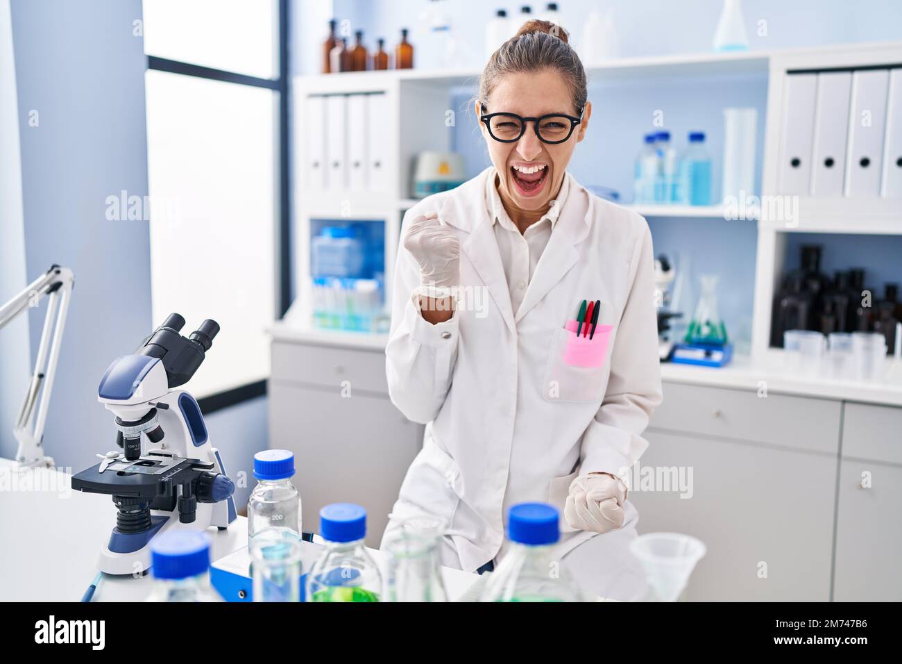 Young woman working at scientist laboratory celebrating surprised and ...