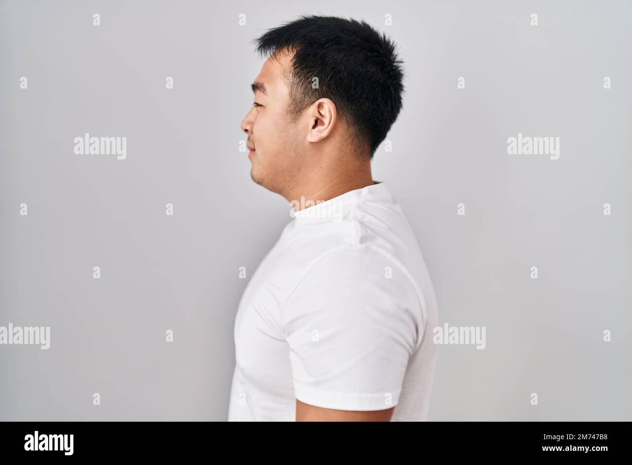 Young chinese man standing over white background looking to side, relax ...