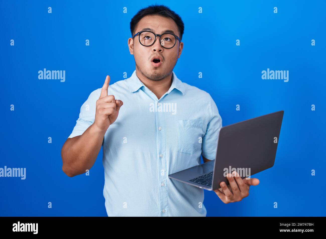 Chinese young man using computer laptop amazed and surprised looking up ...