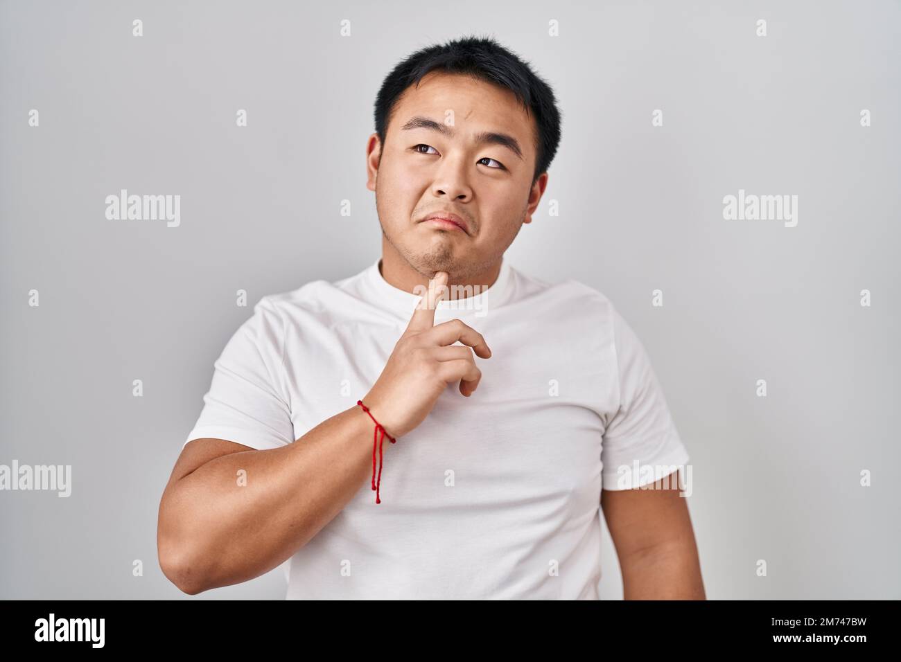 Young chinese man standing over white background thinking concentrated ...