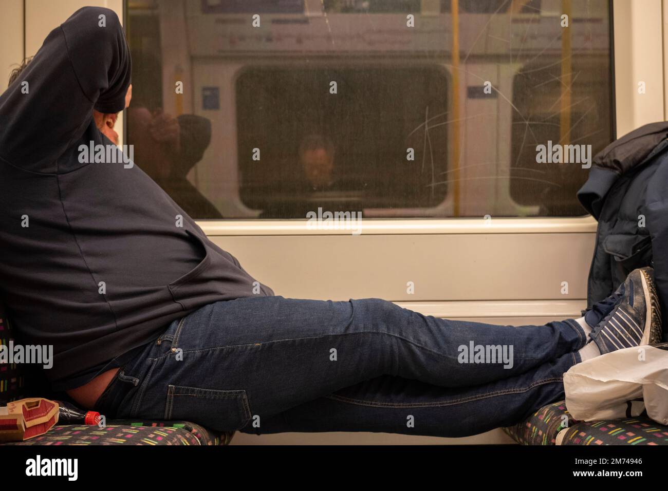 A London Underground tube passenger rests his dirty trainers on seating ...
