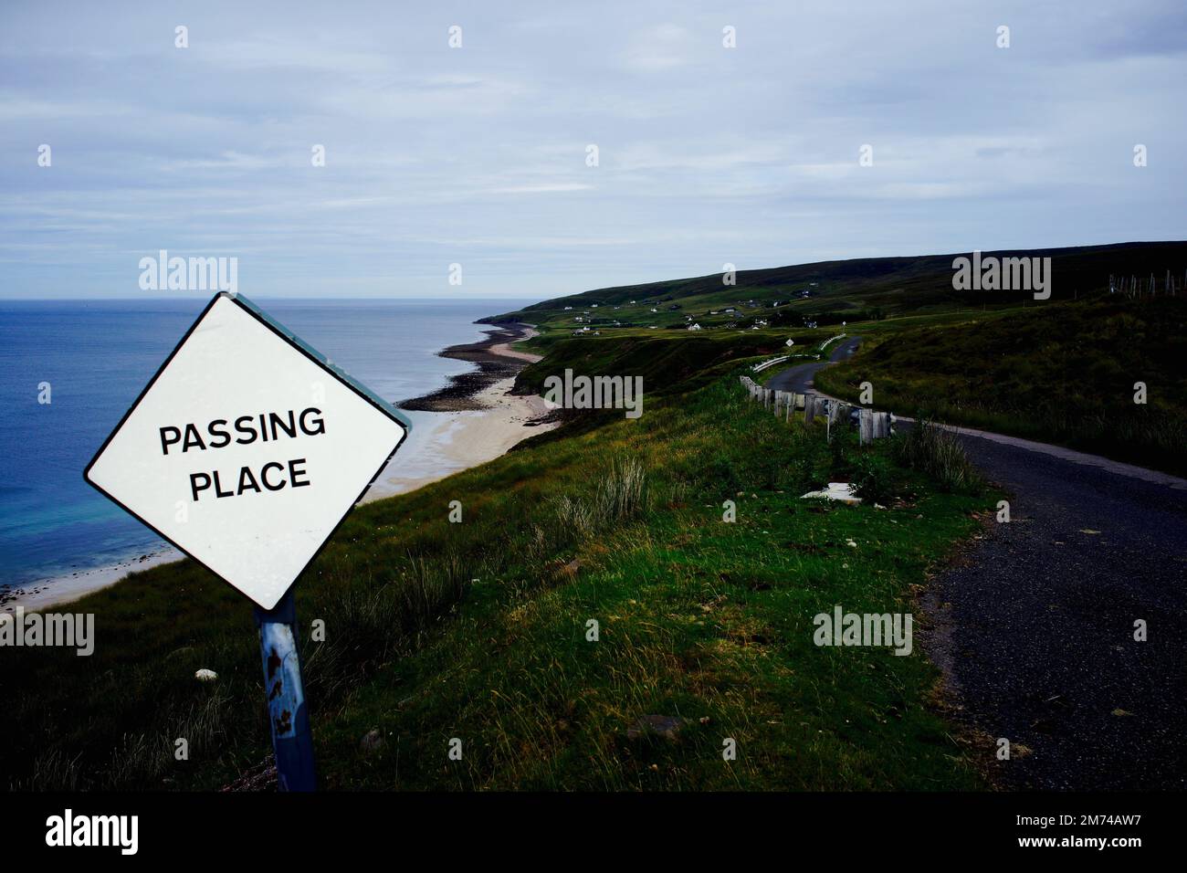 A passing place sign on the shore with a view of the sea on a rainy day ...