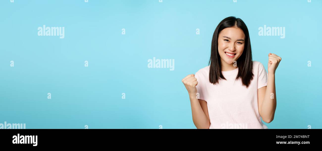 Enthusiastic cute asian girl winning, rejoicing from great news ...