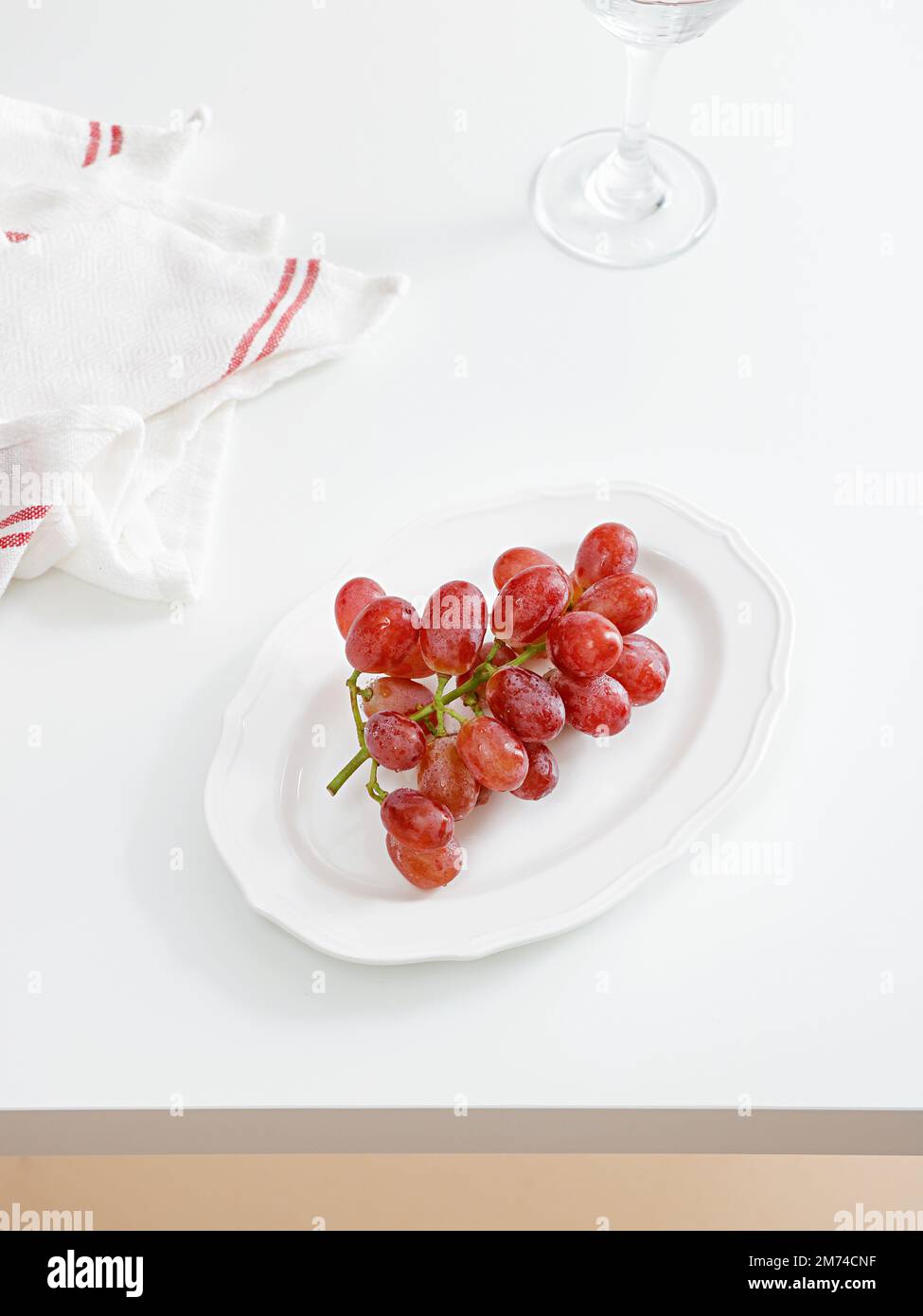 A vertical shot of red grape in a white plate with a kitchen towel on a ...