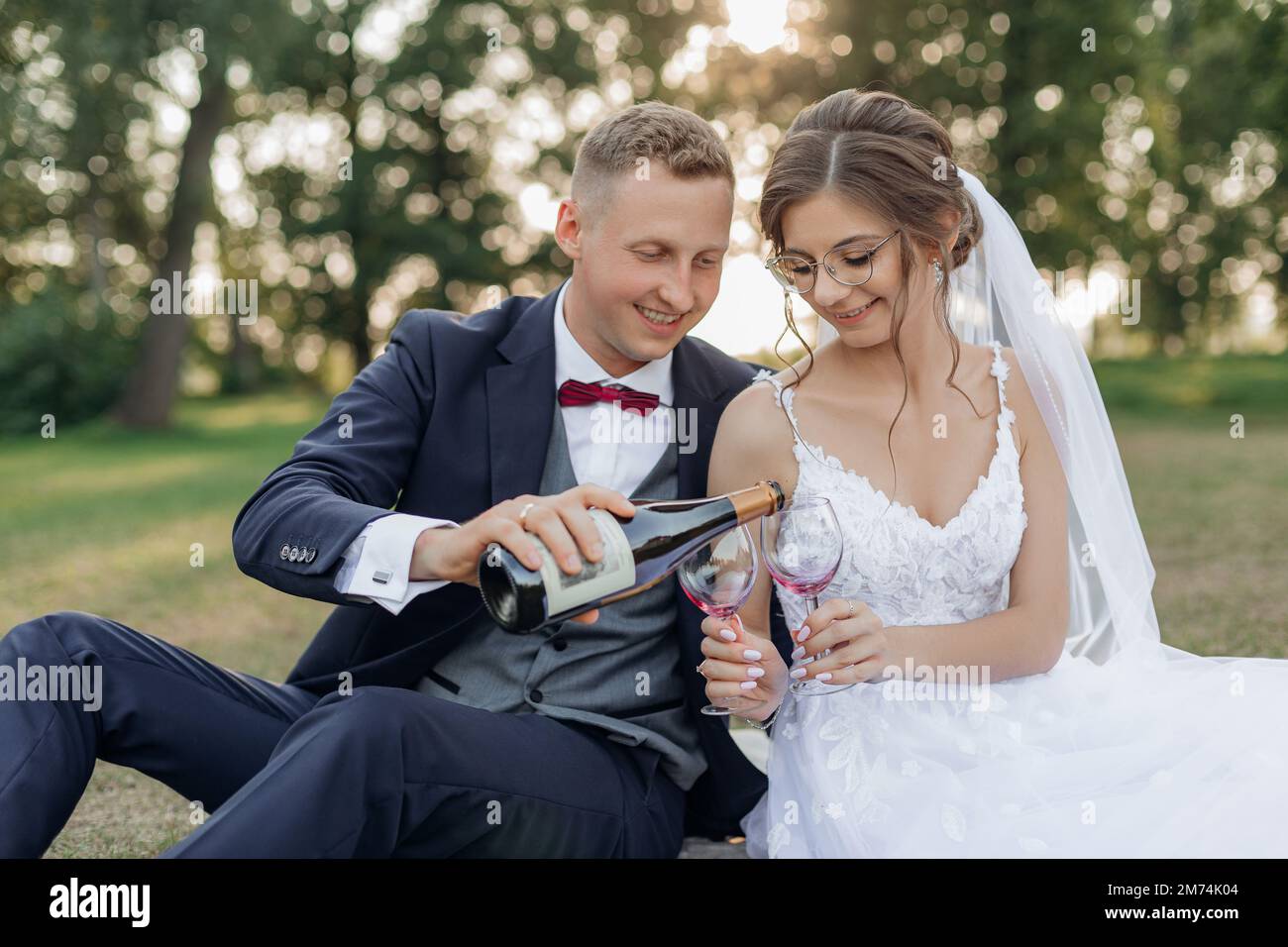 Smiling and shy groom and bride drinking and pouring bubbly champagne ...