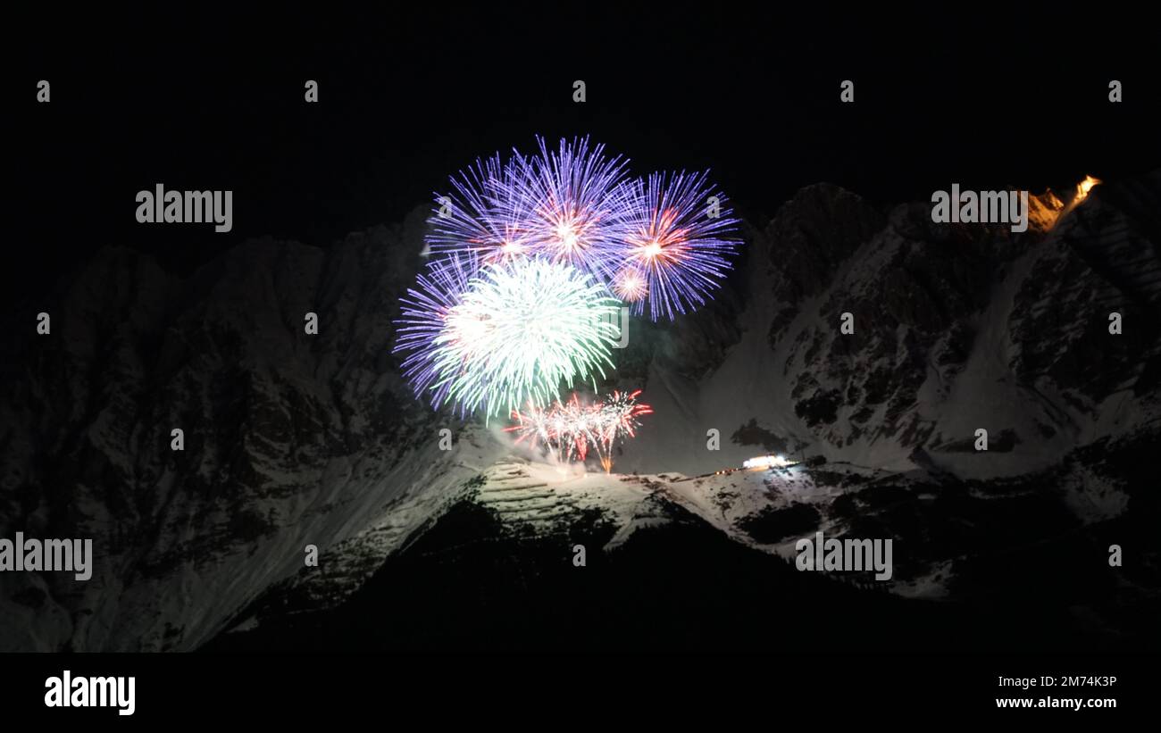 An aerial shot of colorful fireworks on the summit of a snow-covered ...