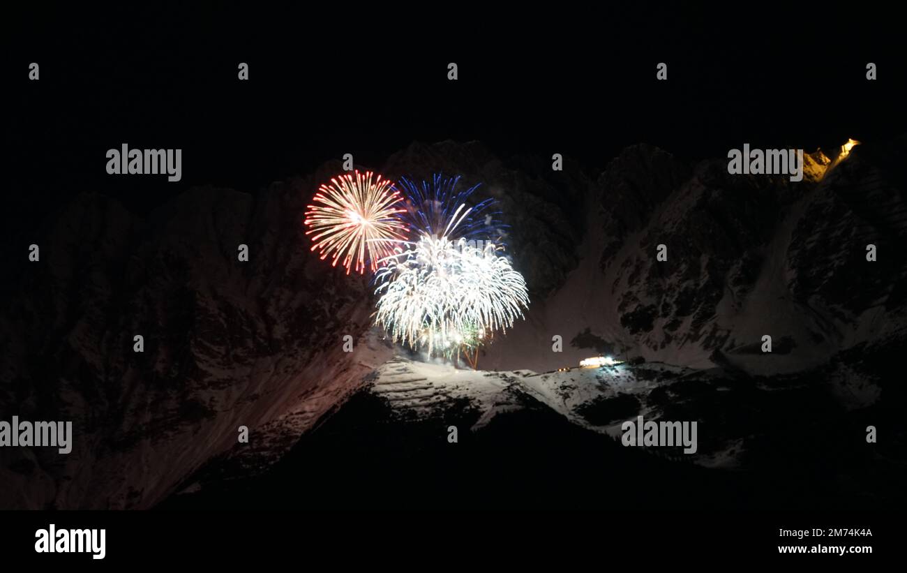 An aerial shot of colorful fireworks on the summit of a snow-covered ...