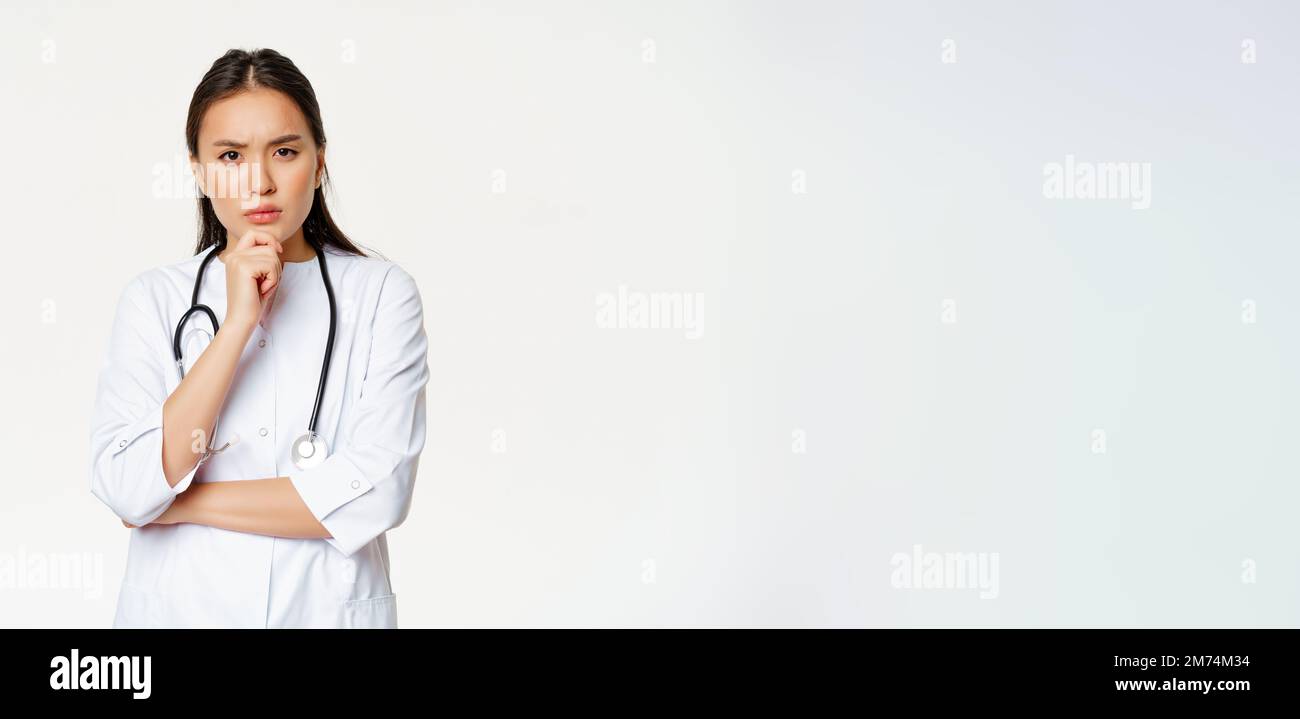 Asian female doctor in uniform thinking, looking serious and concerned ...