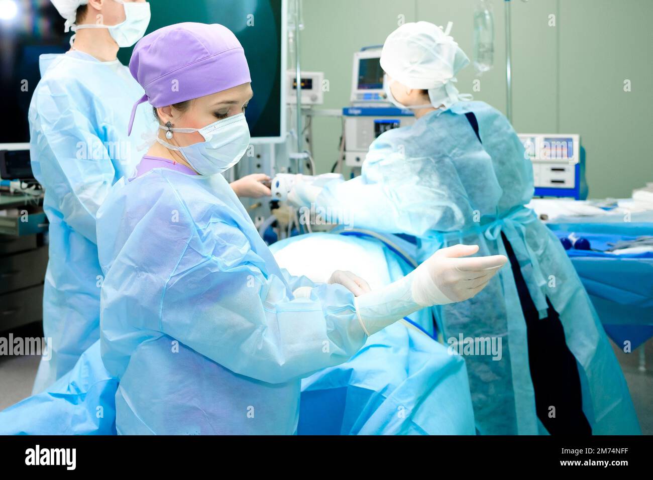 A female surgeon pulls sterile gloves on her hand in the operating room ...