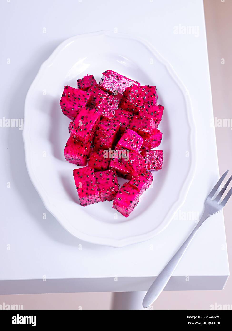 A vertical shot of pink dragon fruit cut in cubes in a white plate with ...