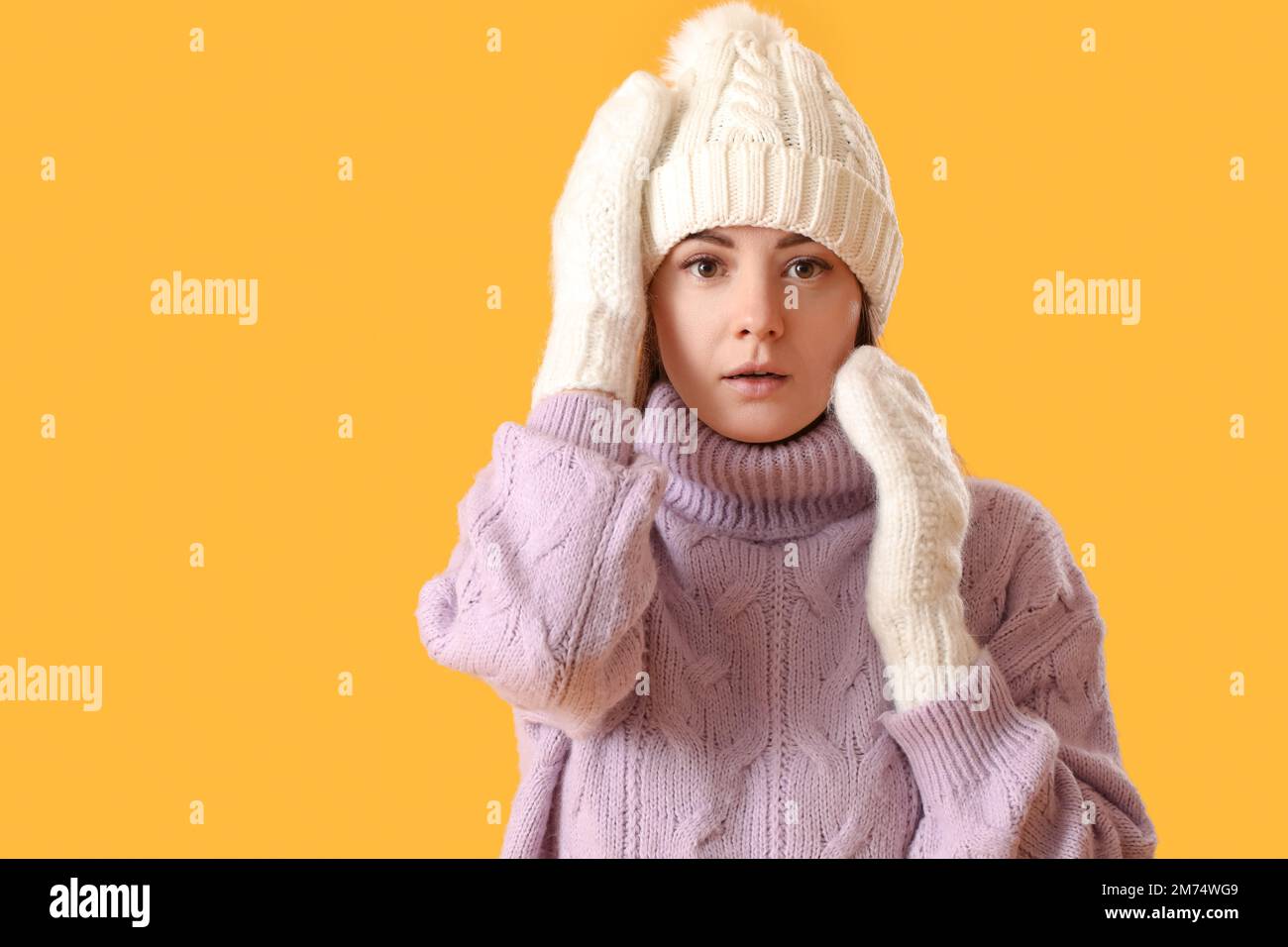 Frozen young woman in winter clothes on yellow background, closeup ...