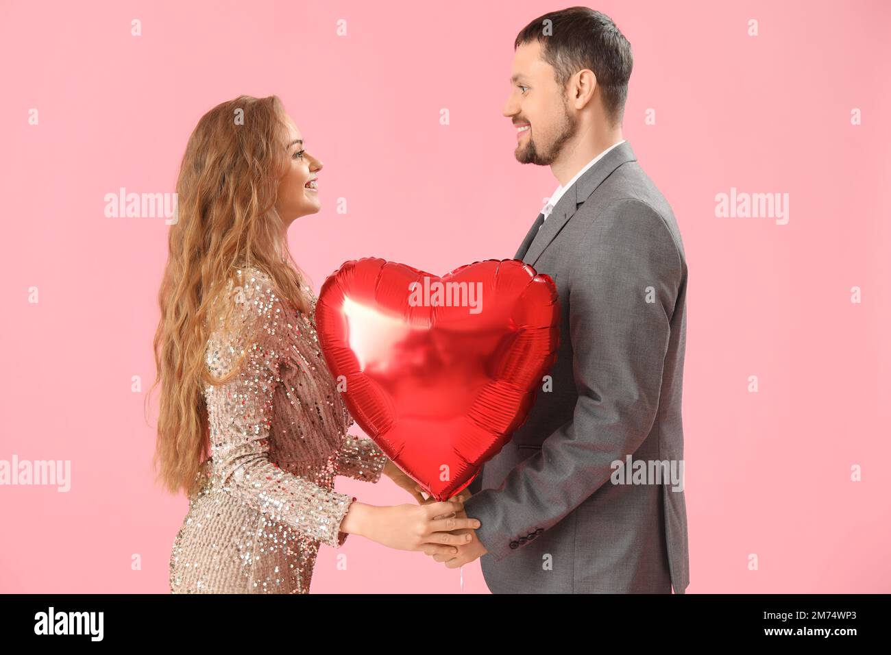 Happy young couple with heart-shaped balloon on pink background ...