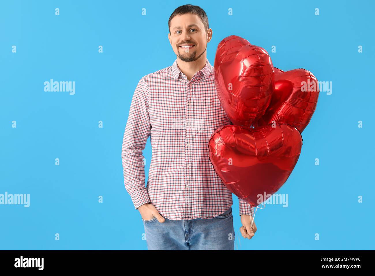 Handsome man with heart-shaped balloons on light blue background ...