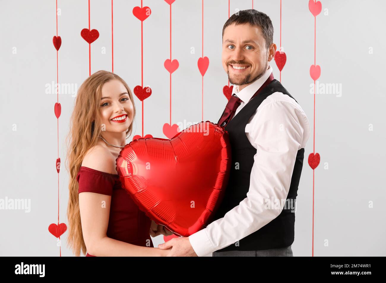 Happy young couple with heart-shaped balloon on light background ...
