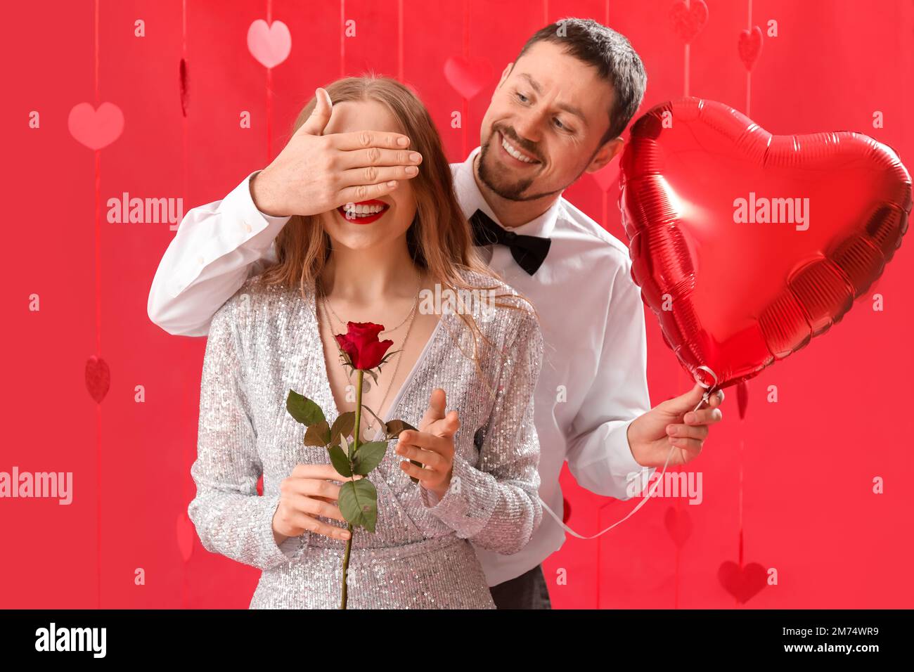 Happy young couple with heart-shaped balloon and rose on red background ...