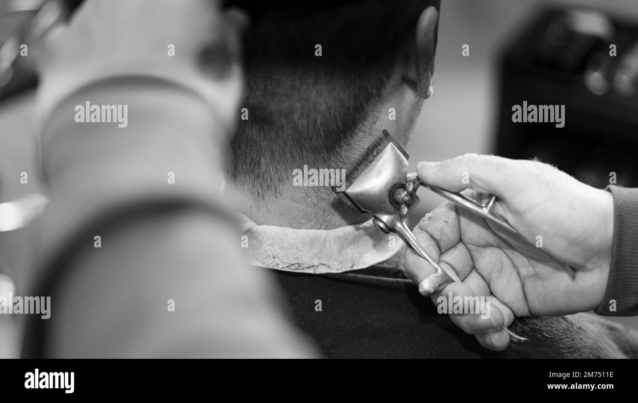 A close-up shot of the hands of a barber with a hair clipper doing a ...