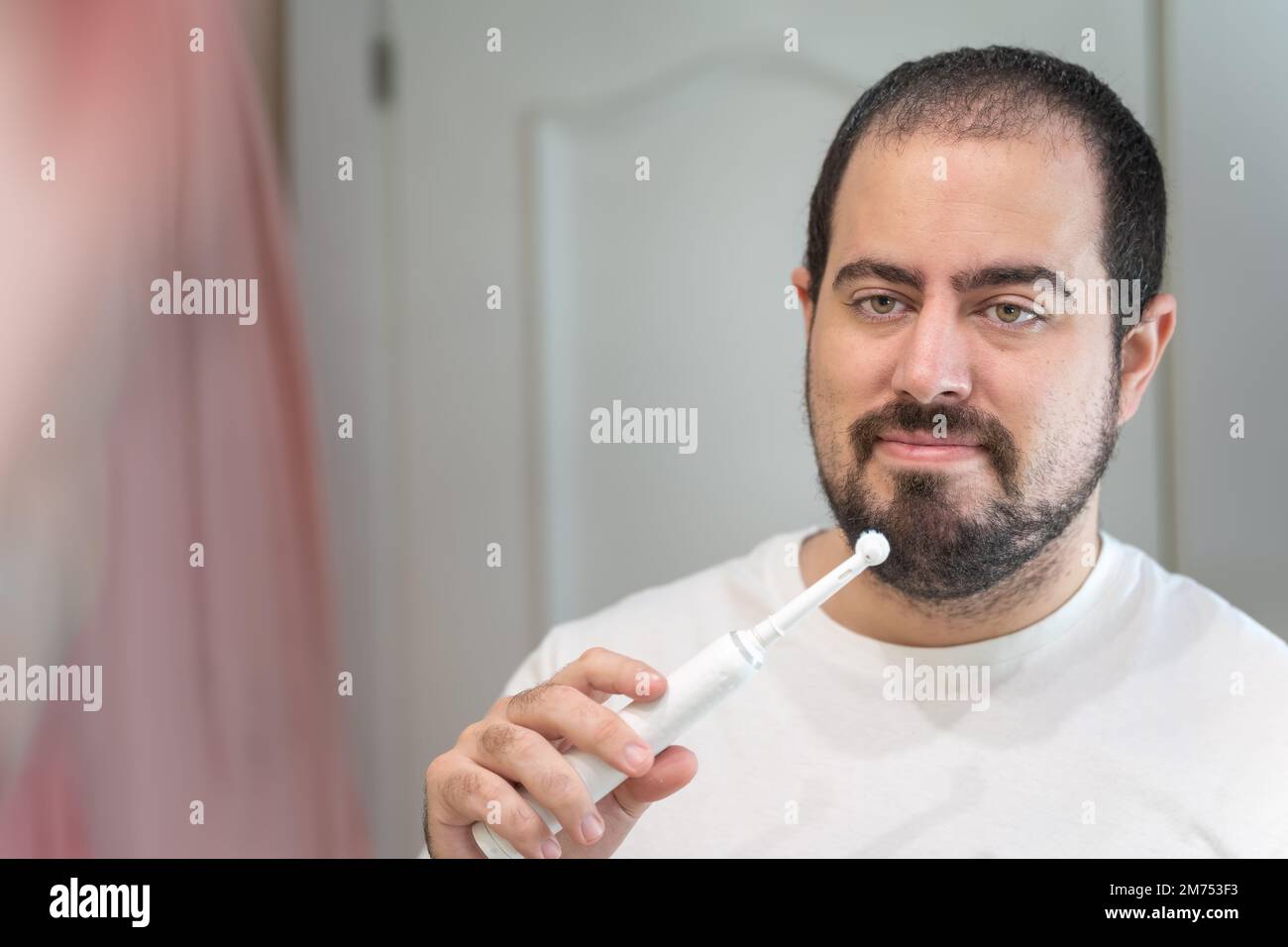 Young white man with a beard and a toothbrush, looking at the bathroom ...