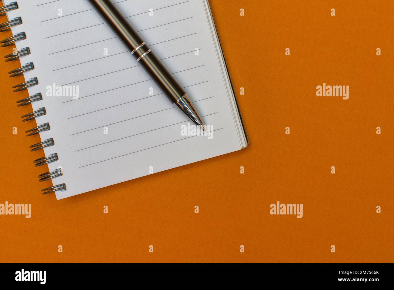 A notebook with a blank page and a pen resting on it On orange matte ...