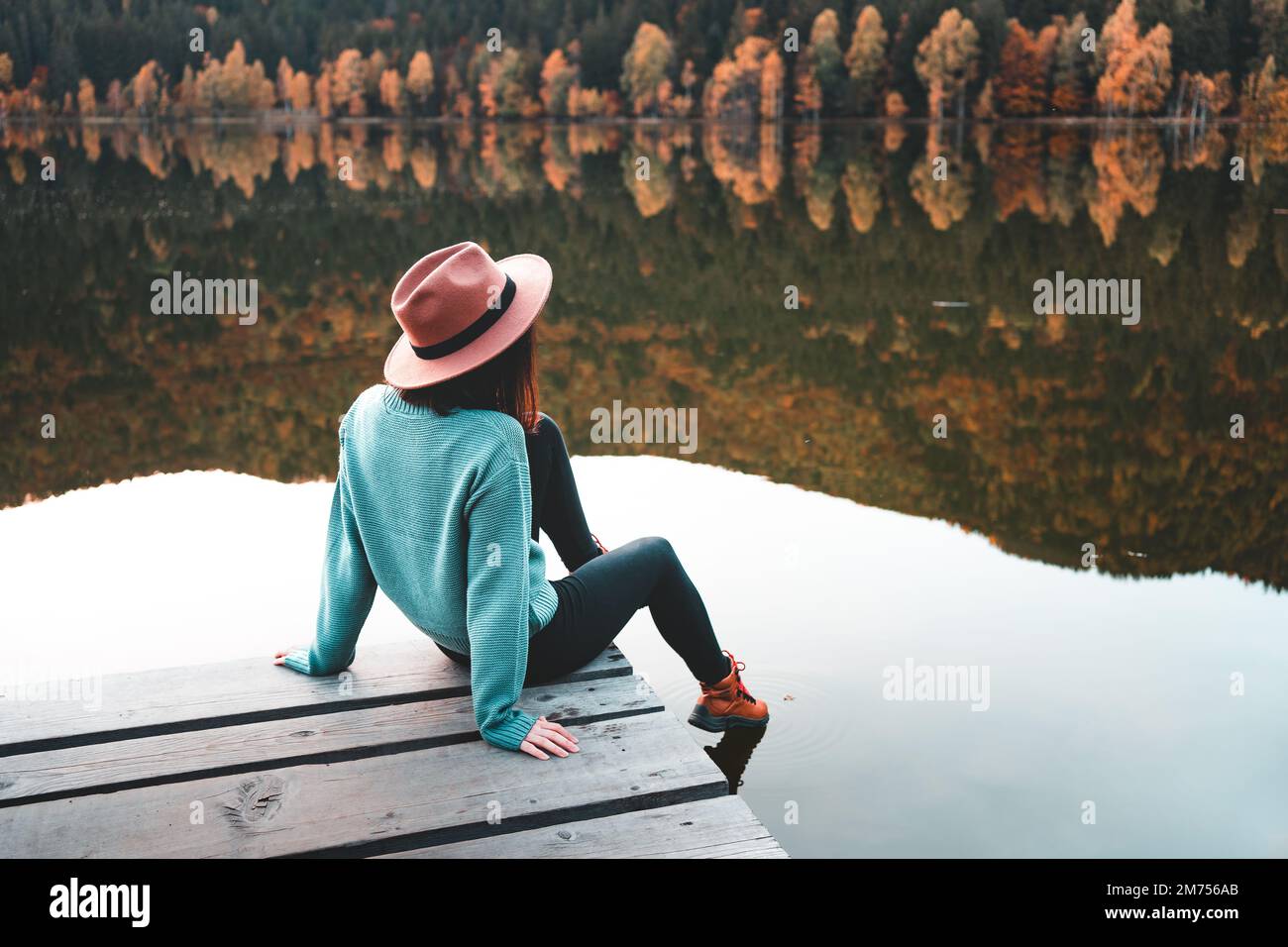 Side view of fashioned young woman sitting on wooden dock against ...