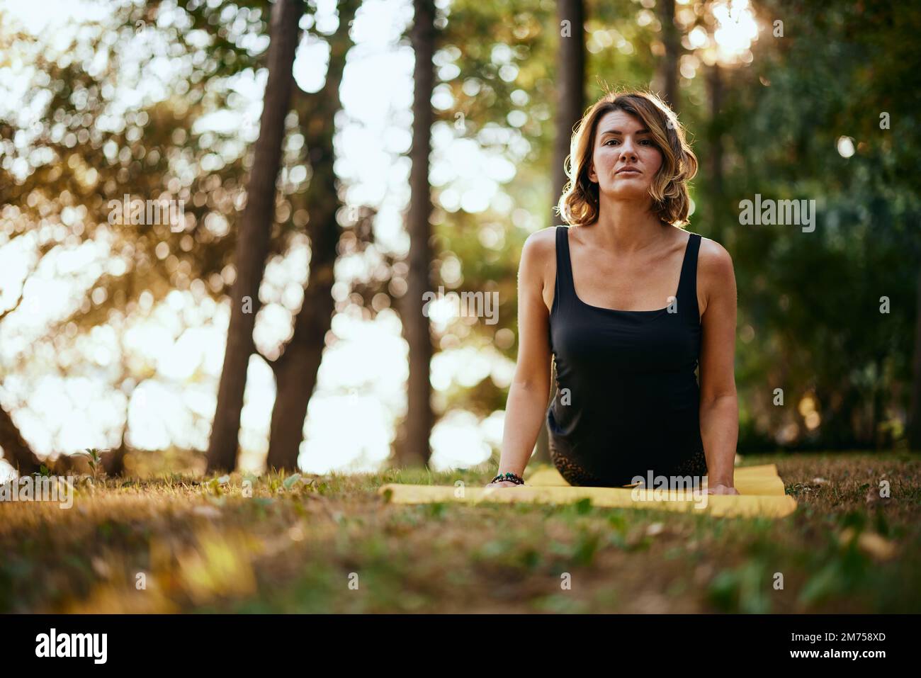 A slim yogi woman practicing yoga in the forest. She is in a cobra yoga ...