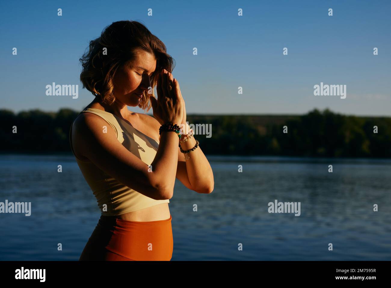 A fit yogi woman is standing near the river in nature and doing sun ...