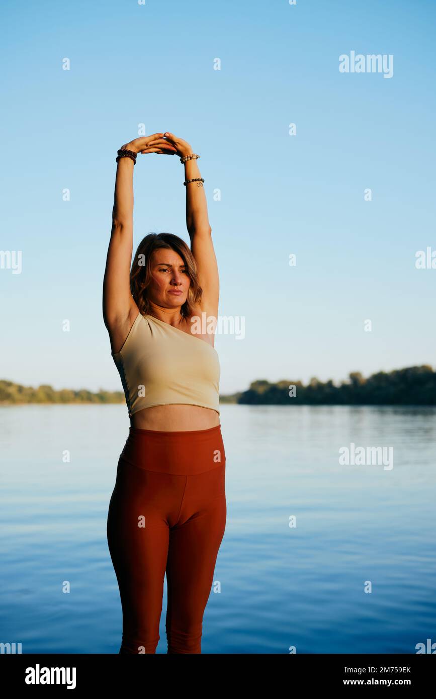 A yogi woman stretches on the dock and prepares for sun salutation ...