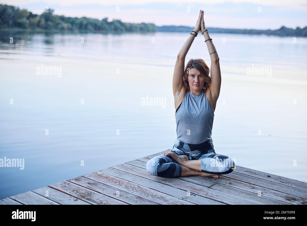 A calm woman in the lotus pose sits on a dock and practices yoga ...