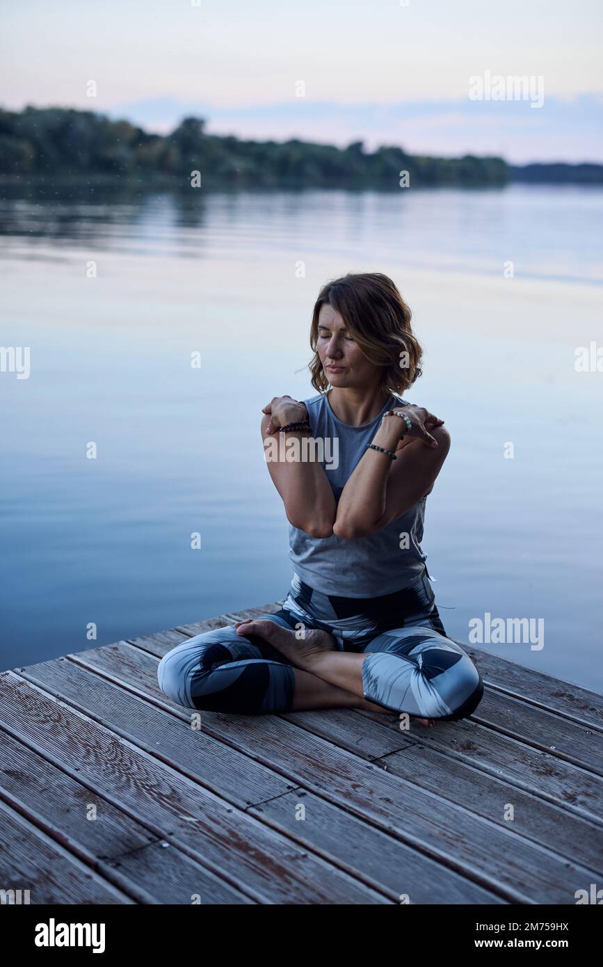 A calm yogi woman in a lotus position is meditating on the dock Stock ...