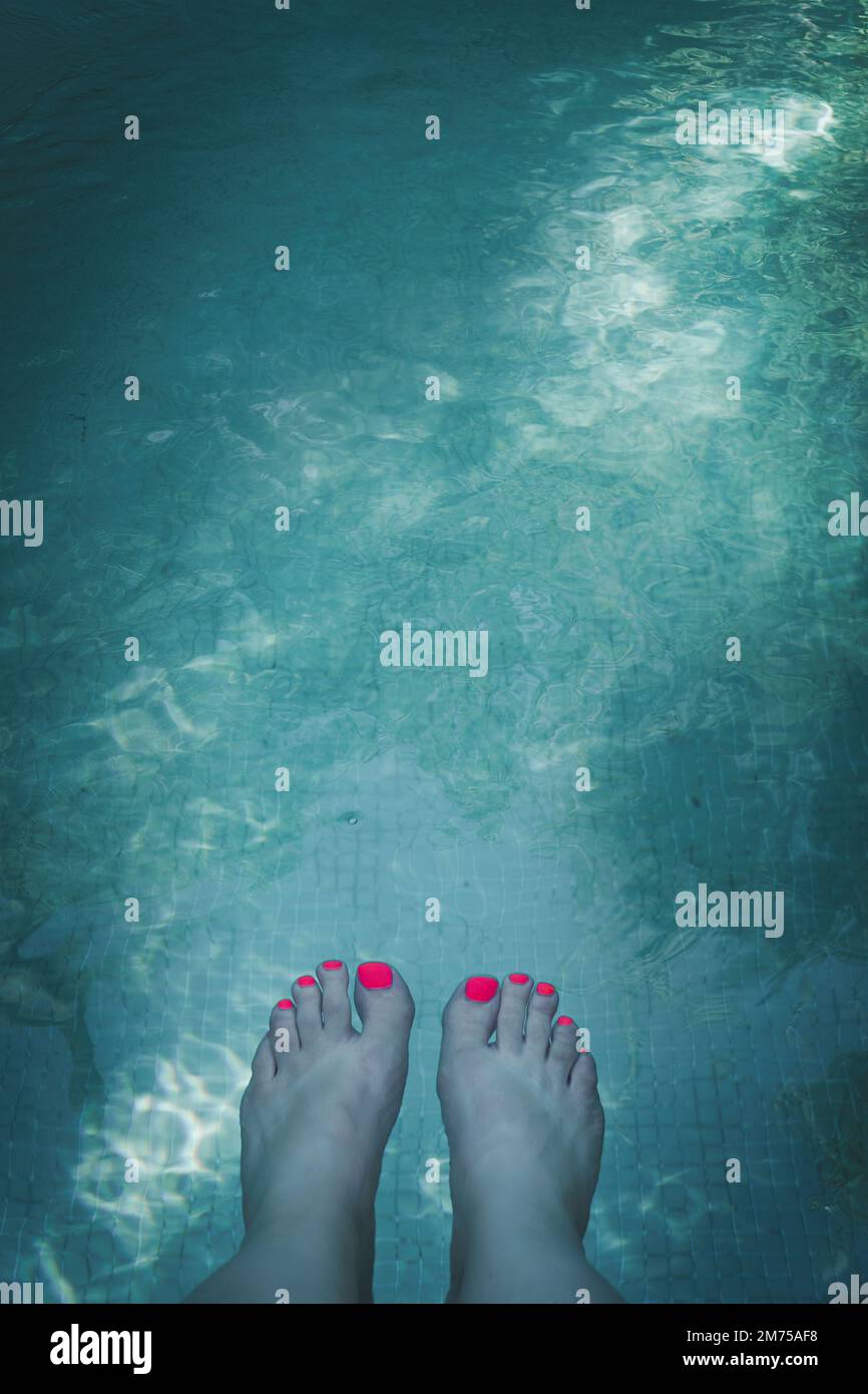 Womans feet in swimming pool of bright turquoise blue water. Vivid pink ...