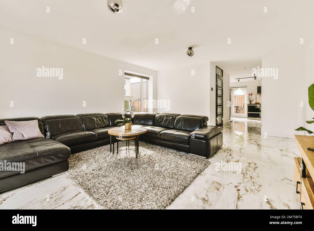 a living room with black leather couches and white marble flooring in ...