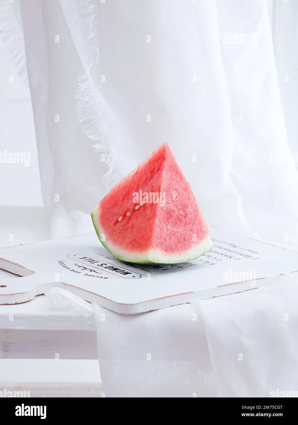A vertical shot of a slice of watermelon on a white wooden board on a ...
