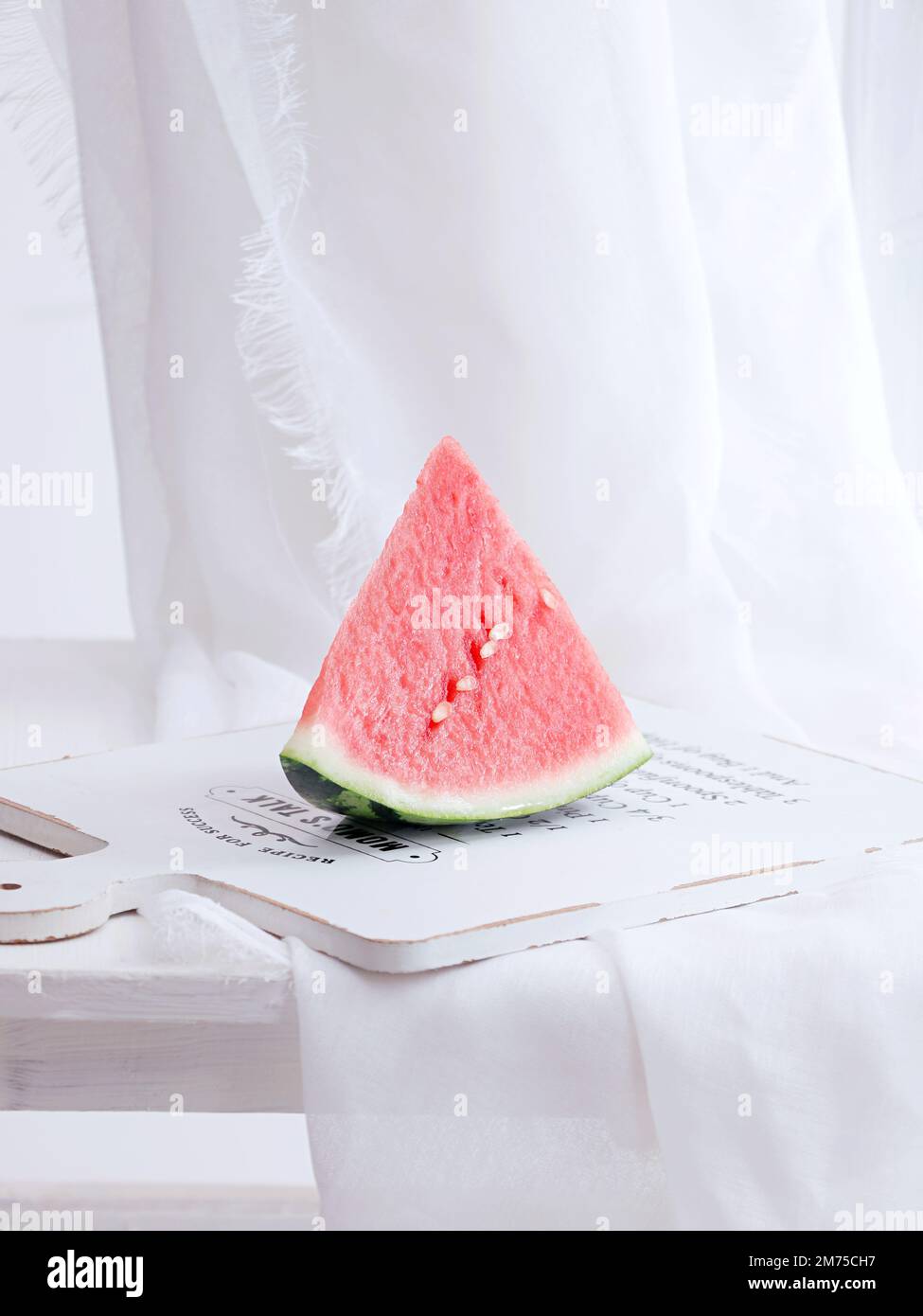 A vertical shot of a slice of watermelon on a white wooden board on a ...