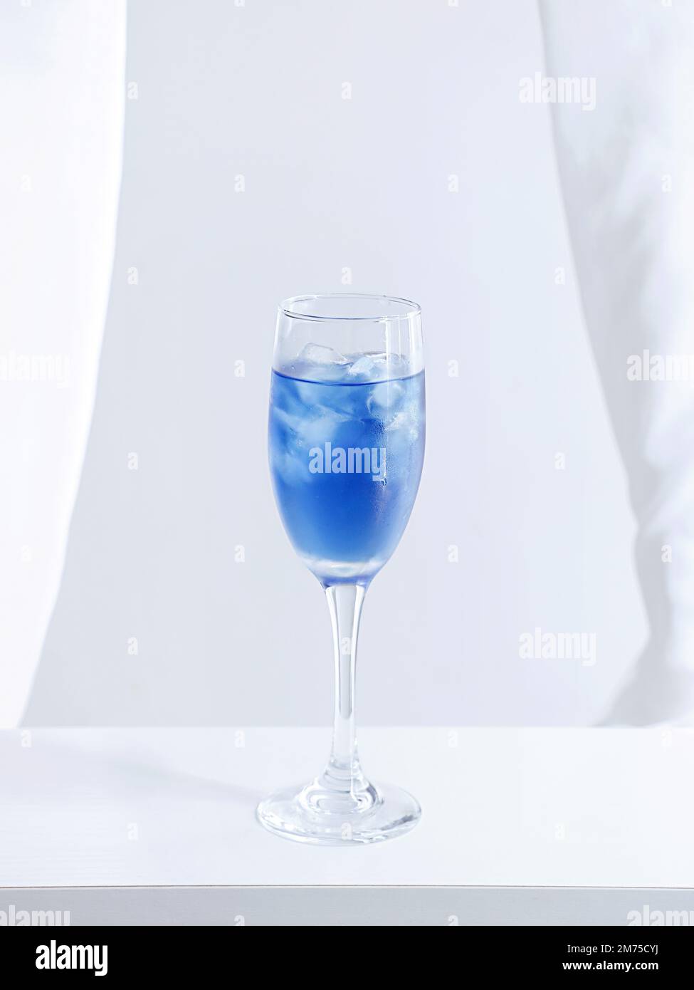 A vertical shot of a blue cocktail juice in a glass on a white surface ...