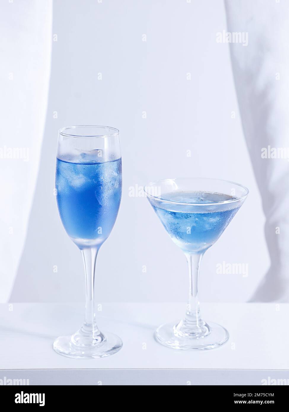 A vertical shot of blue cocktail juice in glasses on a white surface on ...