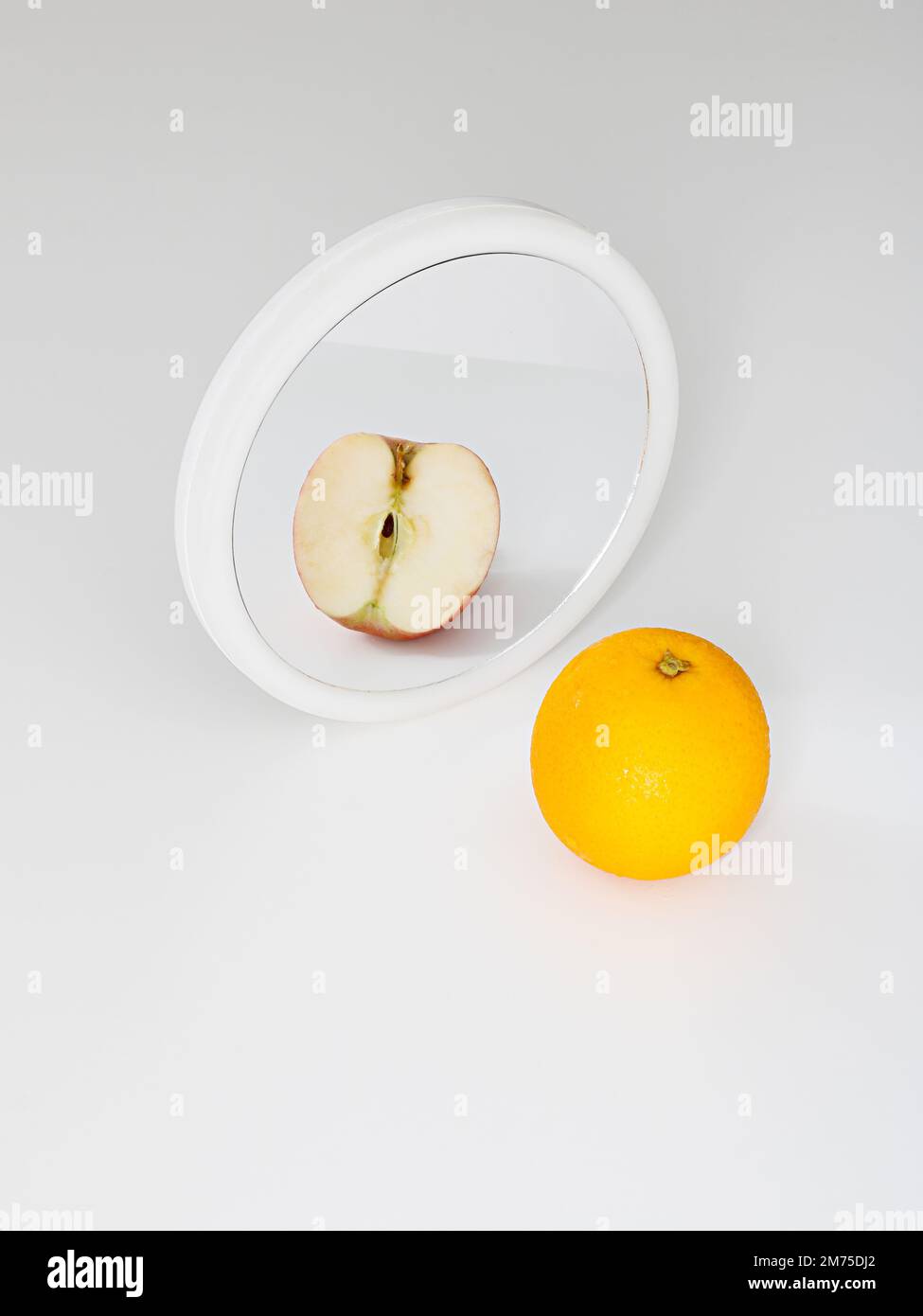 A vertical shot of an orange reflecting in a mirror as a cut red apple ...