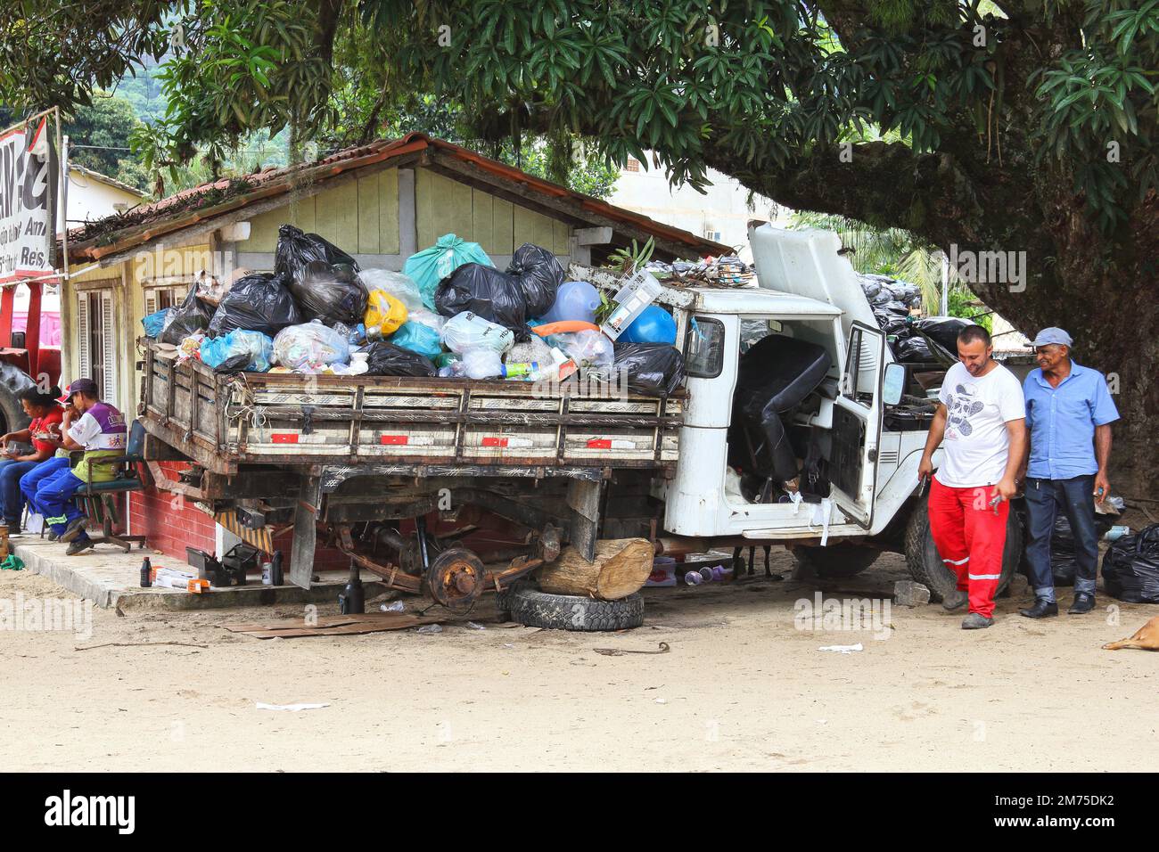 Two men standing by a broken truck filled with garbage at Ilha Bella in ...