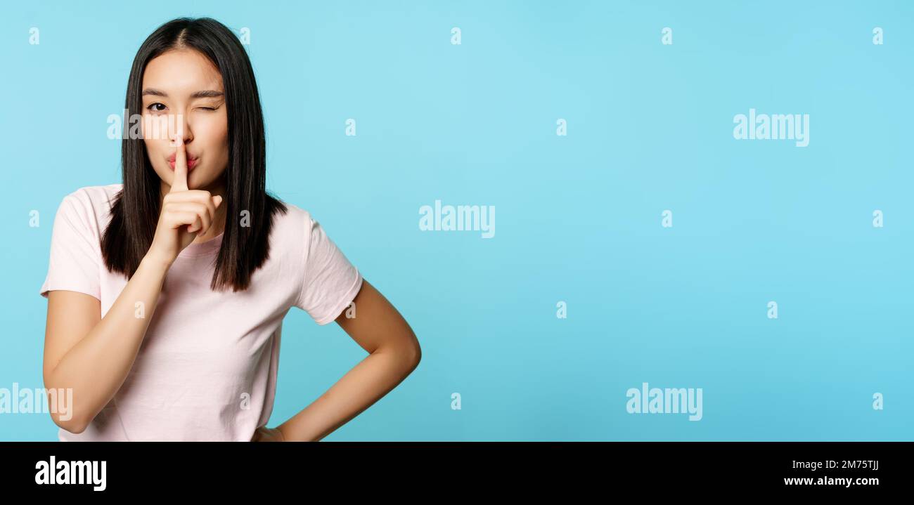 Smiling coquettish asian girl shushing, making silence taboo gesture ...
