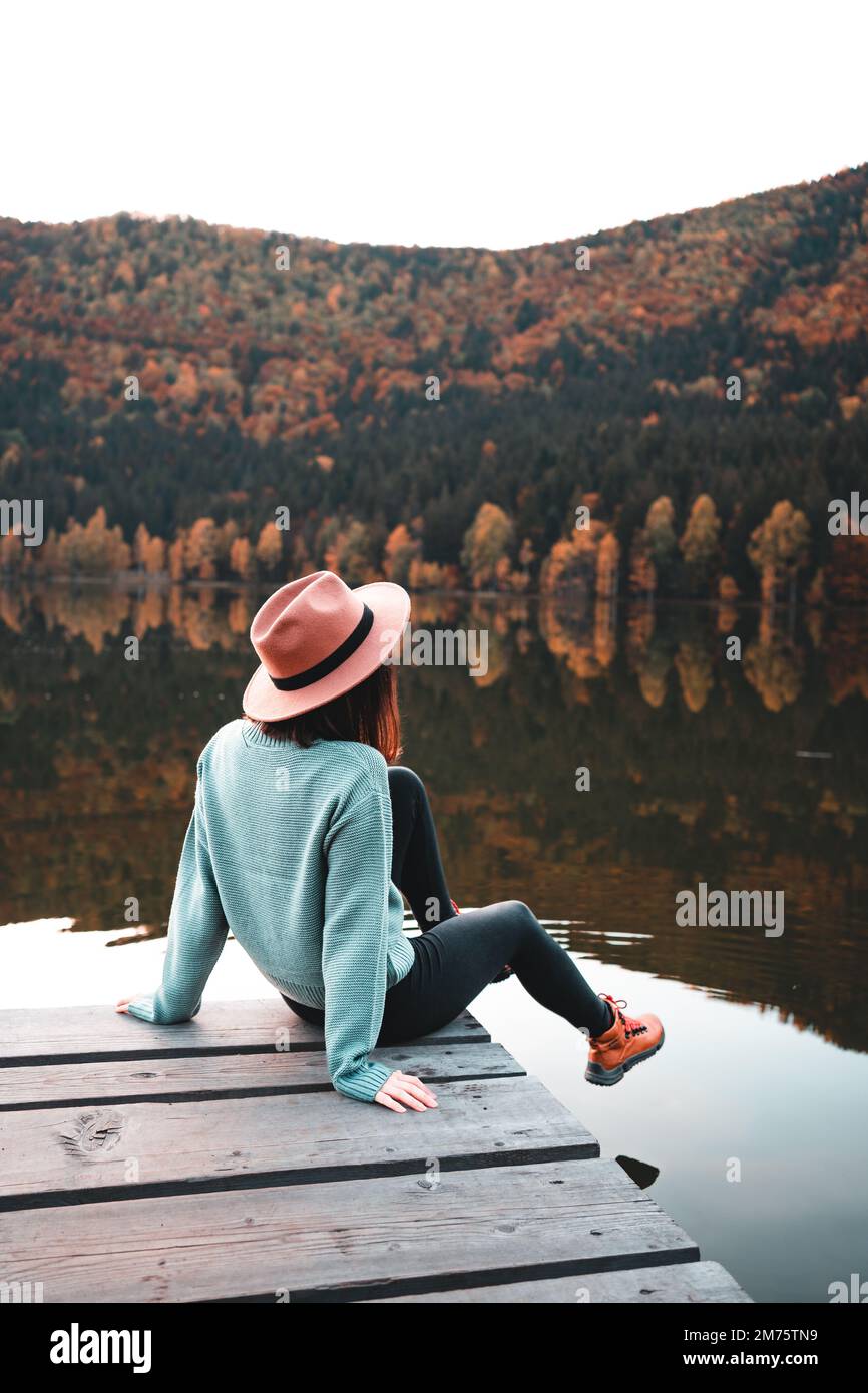 Side view of fashioned young woman sitting on wooden dock Stock Photo ...