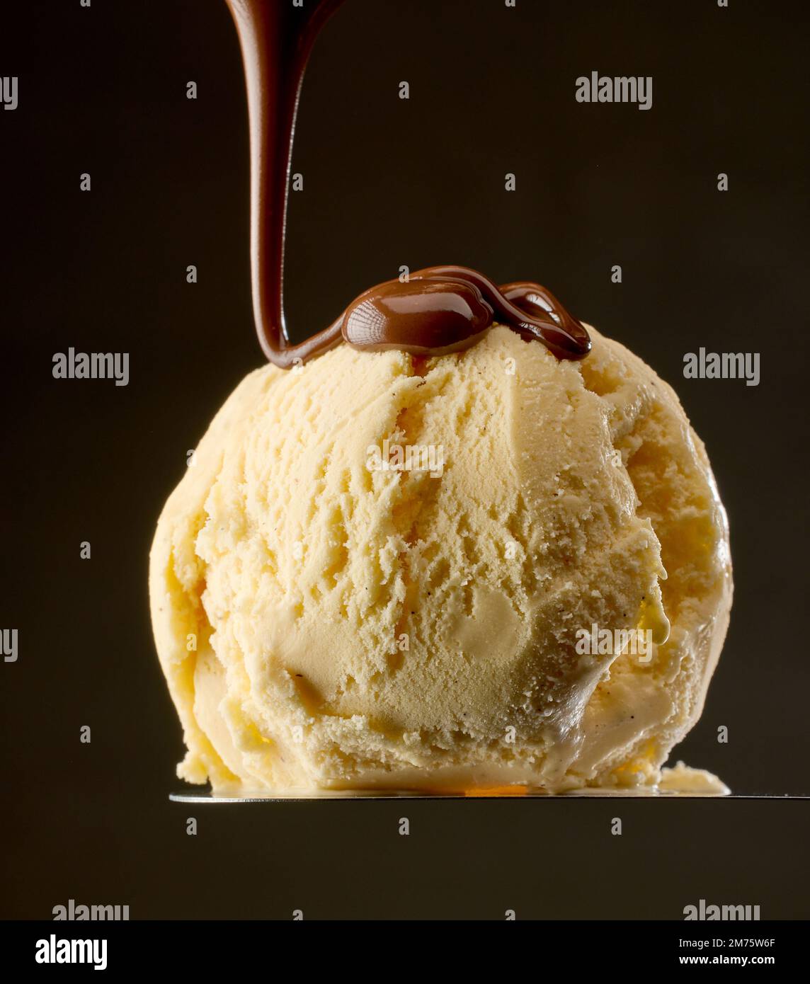 melted chocolate pouring on vanilla ice cream ball on black background ...