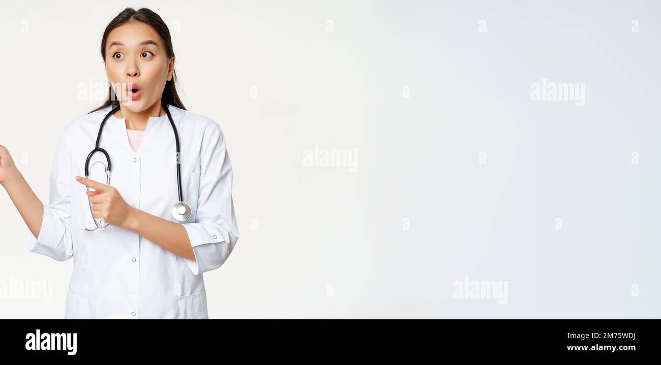 Portrait of enthusiastic female doctor, asian physician pointing and ...