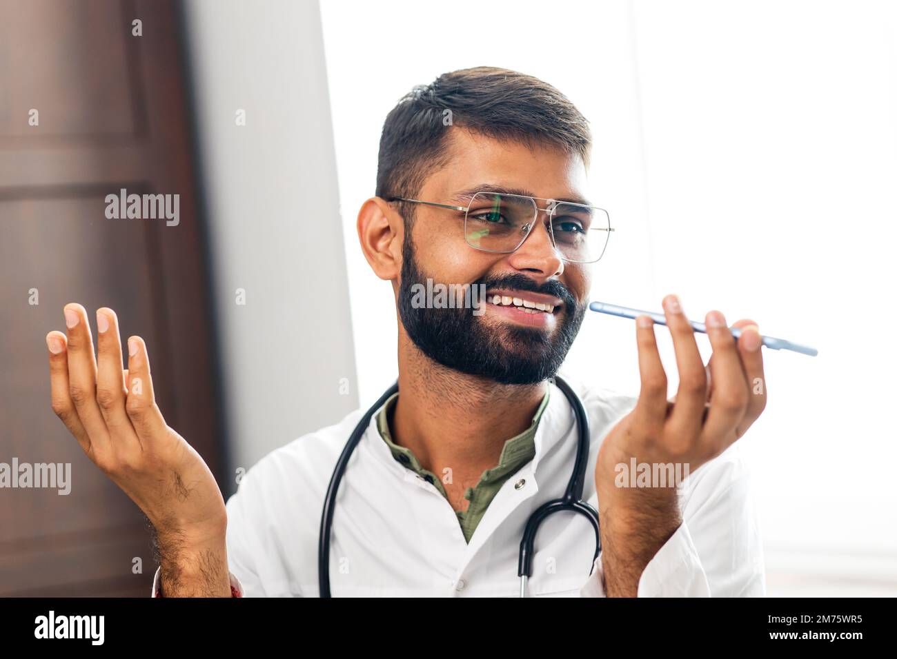 Cheerful indian doctor recording a voice message on mobile phone in ...